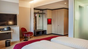 Quarto de hotel moderno com cama, televisão, escrivaninha, cadeira e guarda-roupa.