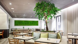 Restaurante moderno com mobiliário de madeira, parede verde e uma grande árvore como peça central.
