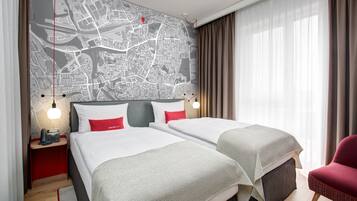 Quarto de hotel com duas camas, um mapa na parede, uma cadeira vermelha e uma mesa de cabeceira com telefone.