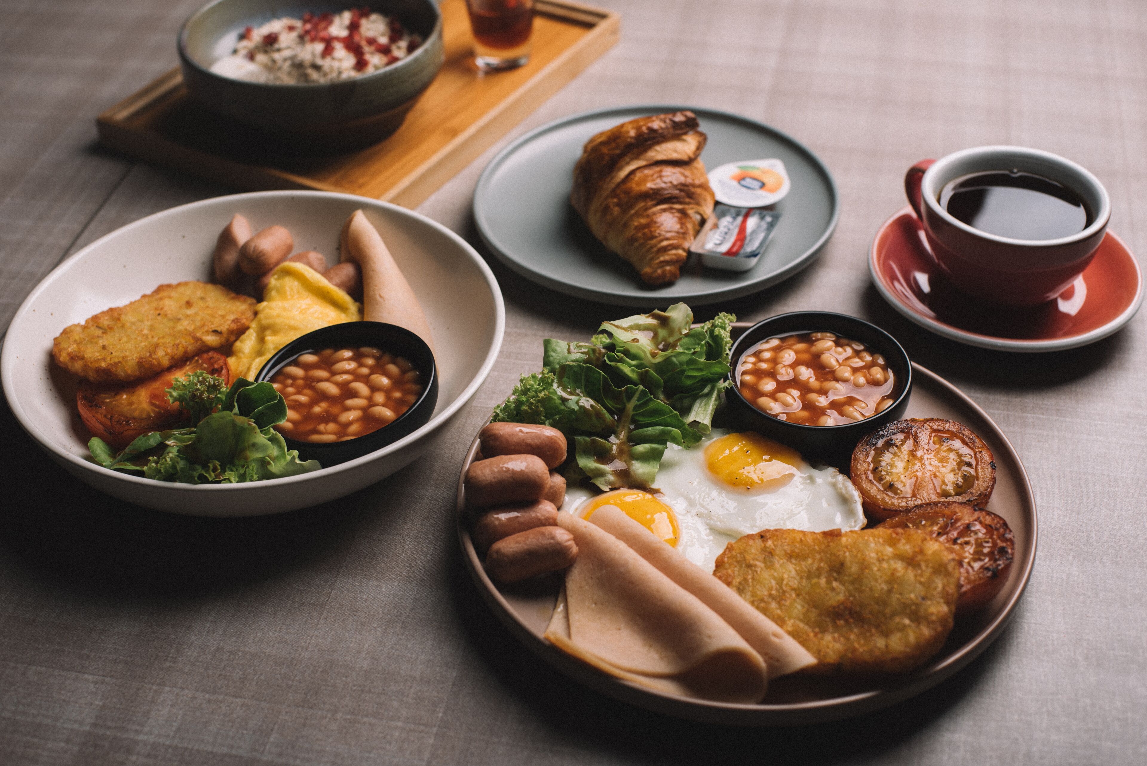 Mesa de café da manhã com diversos pratos, incluindo ovos, linguiça, feijão e torradas.
