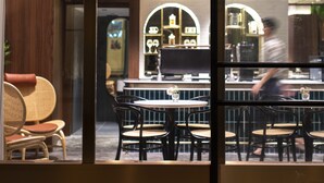 Uma cafeteria com uma placa que diz "FLOW COFFEE". No interior, mesas e cadeiras dispostas para os clientes.
