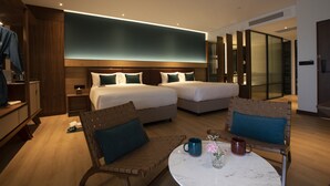 Quarto de hotel moderno com duas camas, uma mesa redonda com um vaso de flores e um espaço de estar com uma cadeira e uma mesa.