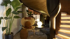 Um interior moderno com uma escada em espiral, uma mesa redonda de madeira com uma luminária esférica e um vaso de planta.