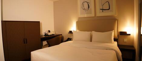 Quarto de hotel com uma cama grande, uma escrivaninha, uma cadeira e duas obras de arte emolduradas na parede.