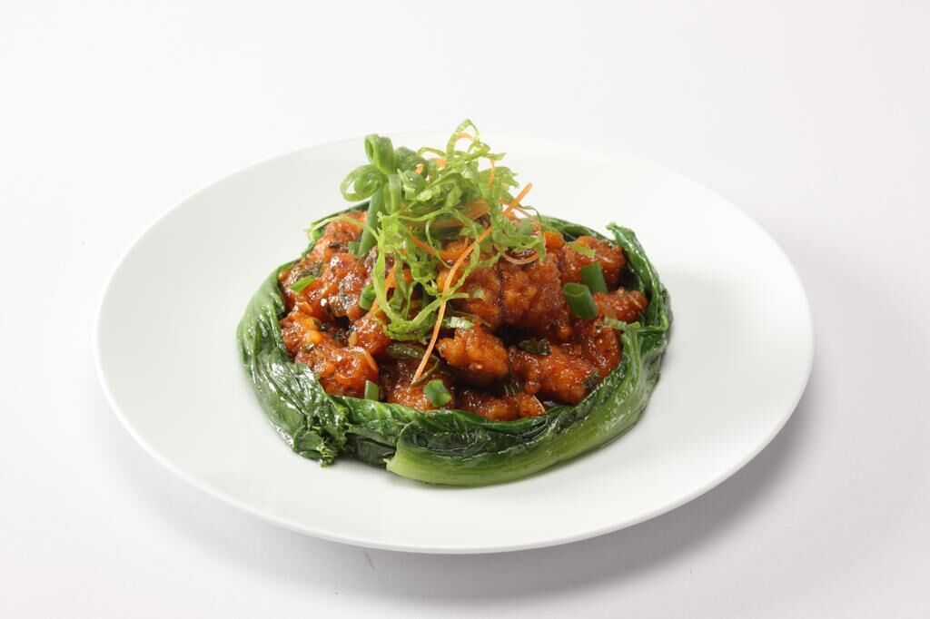 Um prato de comida com uma base de folhas verdes e molho vermelho por cima.