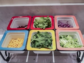 Uma mesa com seis recipientes quadrados, cada um contendo diferentes tipos de comida.
