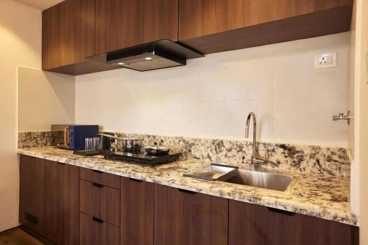 Cozinha com armários de madeira escura, bancada de granito, pia de aço inoxidável e exaustor.