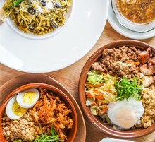 Diversos pratos, incluindo macarrão, uma salada com legumes e carne, e um pote com cenoura ralada e ovo cozido.