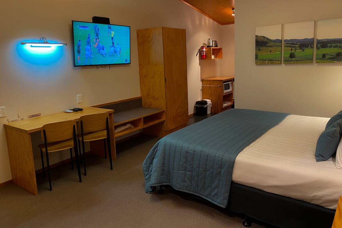 Quarto de hotel com cama, escrivaninha, televisão e vista para a paisagem pela janela.