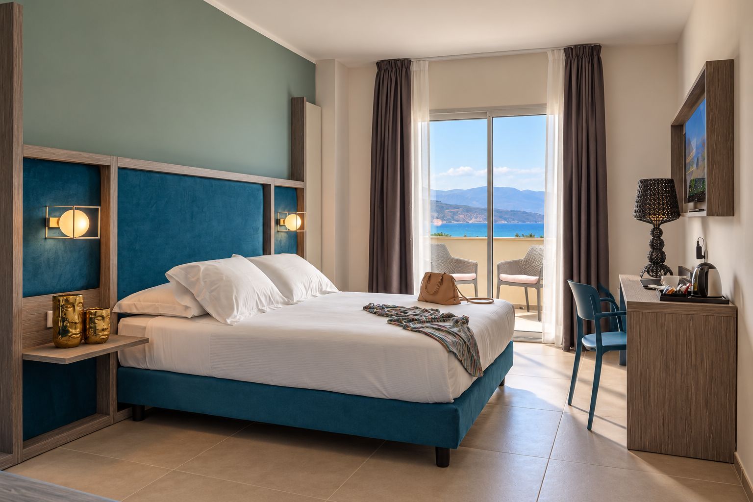 Quarto de hotel com cama, escrivaninha, cadeira, luminária e vista para o mar.