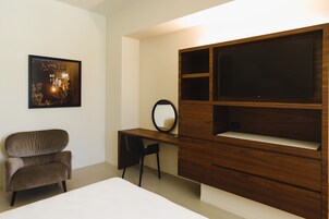 Quarto com cama, escrivaninha com cadeira, televisão e quadro na parede.
