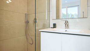 Uma casa de banho moderna com cabine de duche em vidro, lavatório branco e um espelho grande.