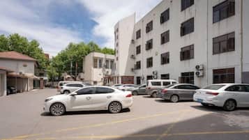 Um estacionamento com vários carros, um edifício com várias janelas e aparelhos de ar condicionado, e um céu claro.