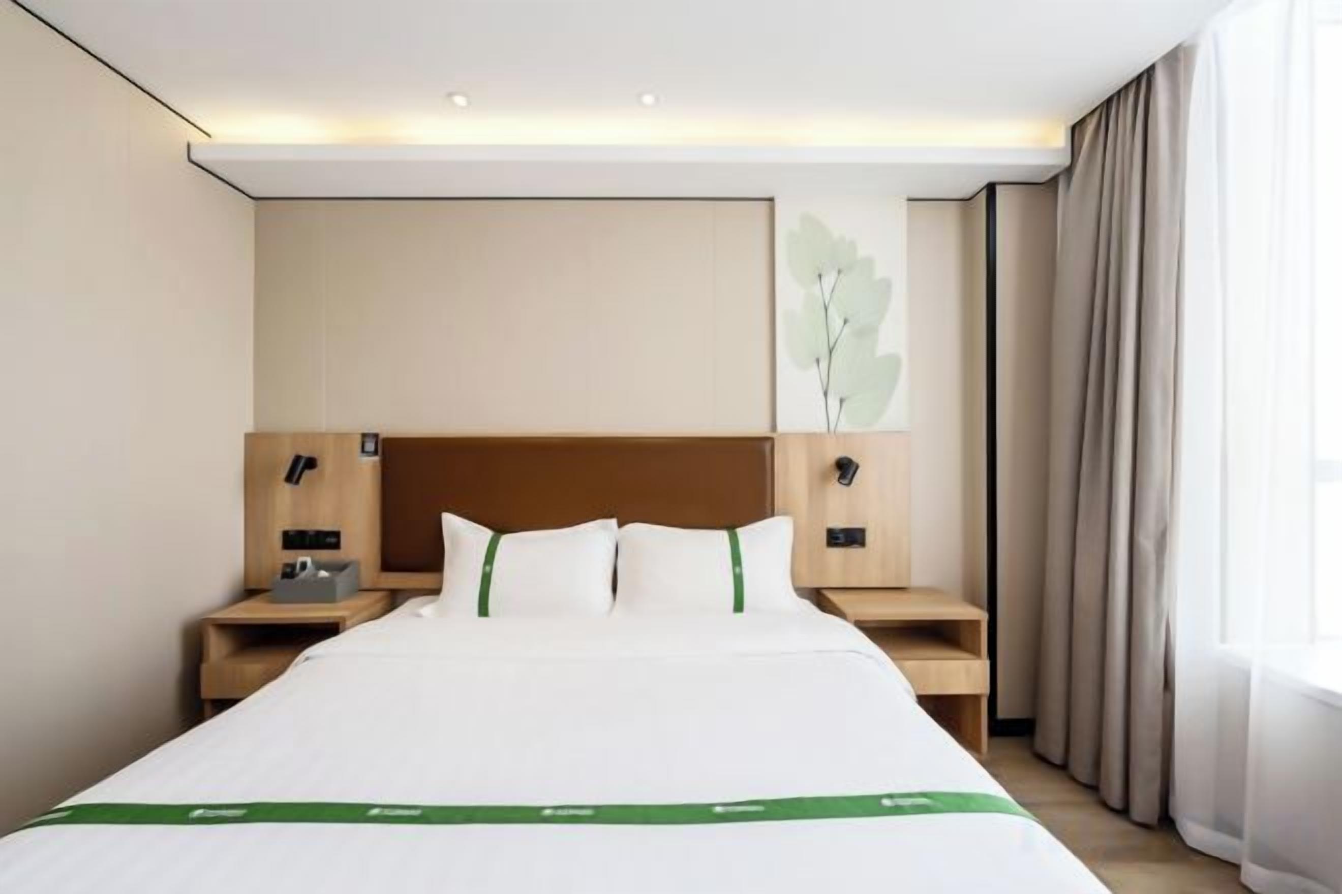 Quarto de hotel com uma cama grande, duas mesas de cabeceira, uma cabeceira e uma janela com cortinas.