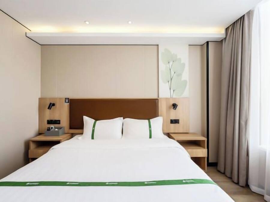 Quarto de hotel com uma cama grande, duas mesas de cabeceira, uma cabeceira e uma janela com cortinas.