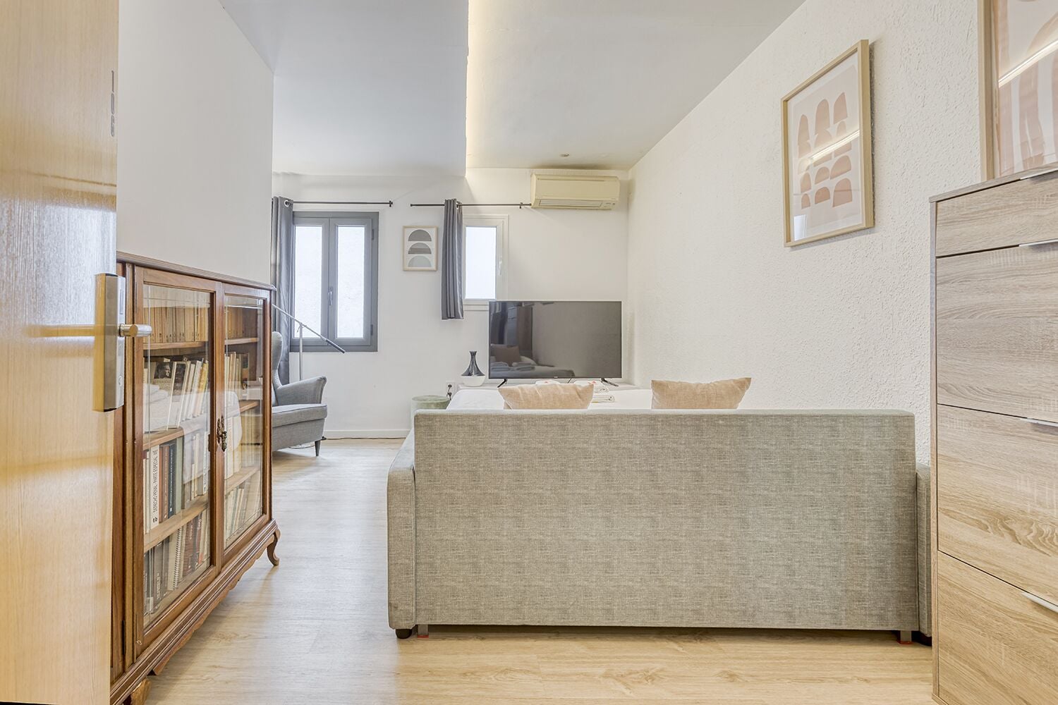 Um espaço de estar compacto com sofá, televisão, armário com livros e janela com cortinas.