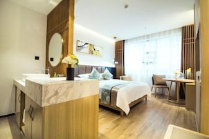 Quarto de hotel com cama, escrivaninha, cadeira, toucador com espelho e janela com cortinas.