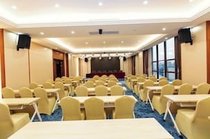 Uma sala de conferências com fileiras de mesas e cadeiras, um palco e uma tela grande.