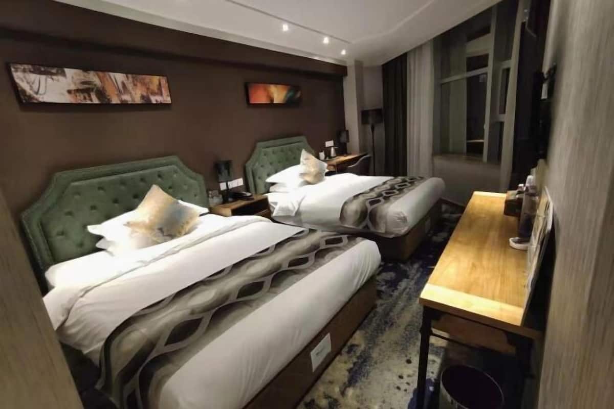 Quarto de hotel com duas camas, uma escrivaninha de madeira, televisão e obras de arte nas paredes.