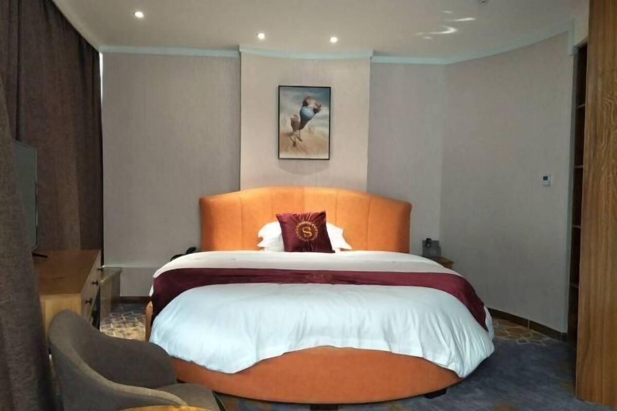 Quarto de hotel com uma cama grande, uma cadeira, uma escrivaninha e um quadro na parede.
