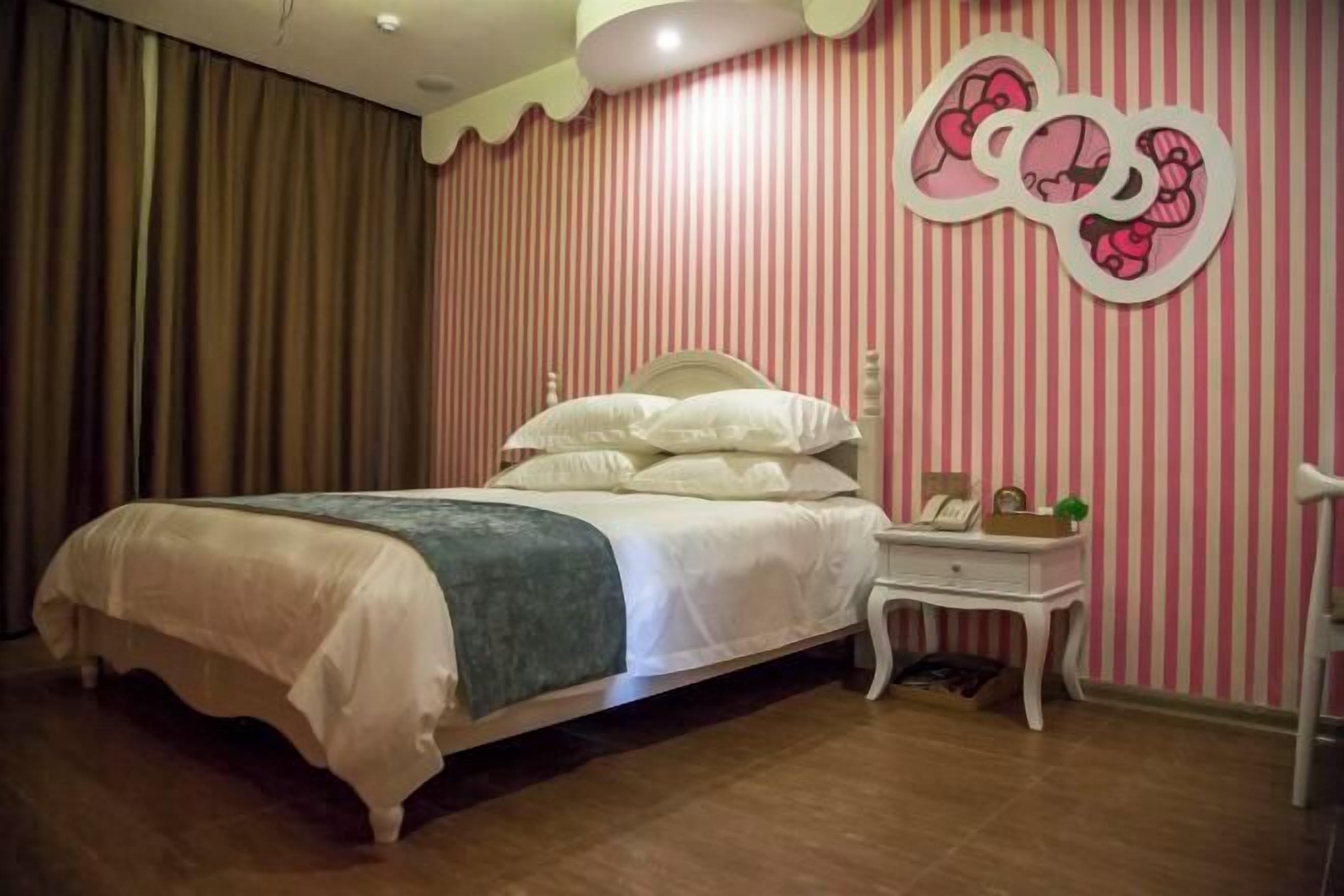 Quarto com cama, mesa de cabeceira, cômoda e parede com papel de parede listrado e um enfeite em formato de coração.