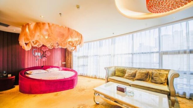 Uma sala de estar moderna com um sofá circular vermelho, um sofá bege, uma mesa de centro de vidro e uma janela grande com cortinas leves.