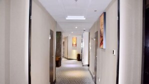 Corredor de hotel com carpete estampado, portas em ambos os lados e teto com iluminação embutida.