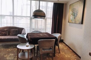 Um quarto com sofá, uma mesa com cadeiras, luminária pendente e uma pintura na parede.