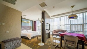Quarto de hotel com uma cama, área de estar com mesa e cadeiras, uma janela grande e um padrão decorativo no chão.