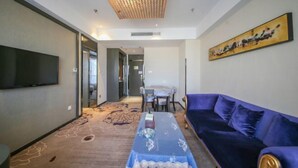 Uma sala de estar moderna com um sofá azul, uma TV de tela plana na parede, um tapete estampado e uma área de refeições com mesa e cadeiras.