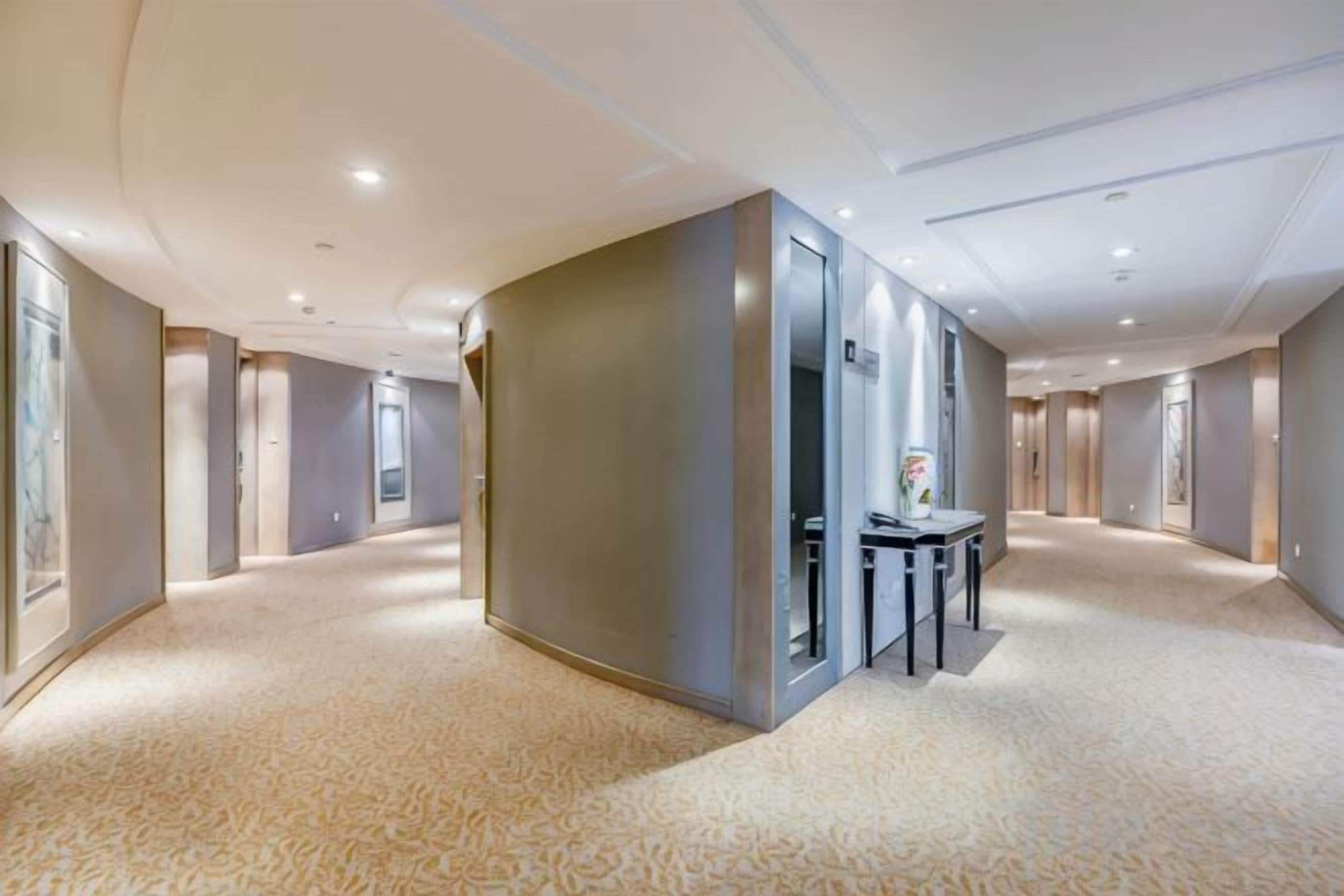 Corredor de hotel com piso carpetado, balcão de recepção e portas de acesso aos quartos.