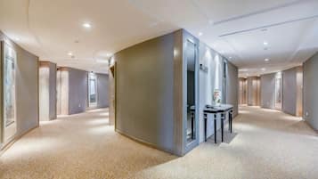 Corredor de hotel com piso carpetado, balcão de recepção e portas de acesso aos quartos.