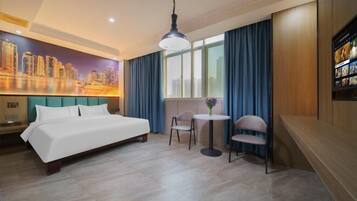 Quarto de hotel com cama, uma mesinha com cadeiras, um mural com vista para a cidade e uma janela grande com cortinas.