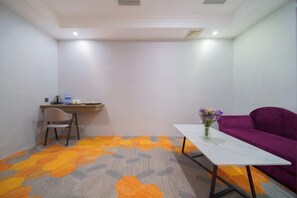 Quarto com escrivaninha, cadeira, sofá roxo e uma mesa com um vaso de flores.