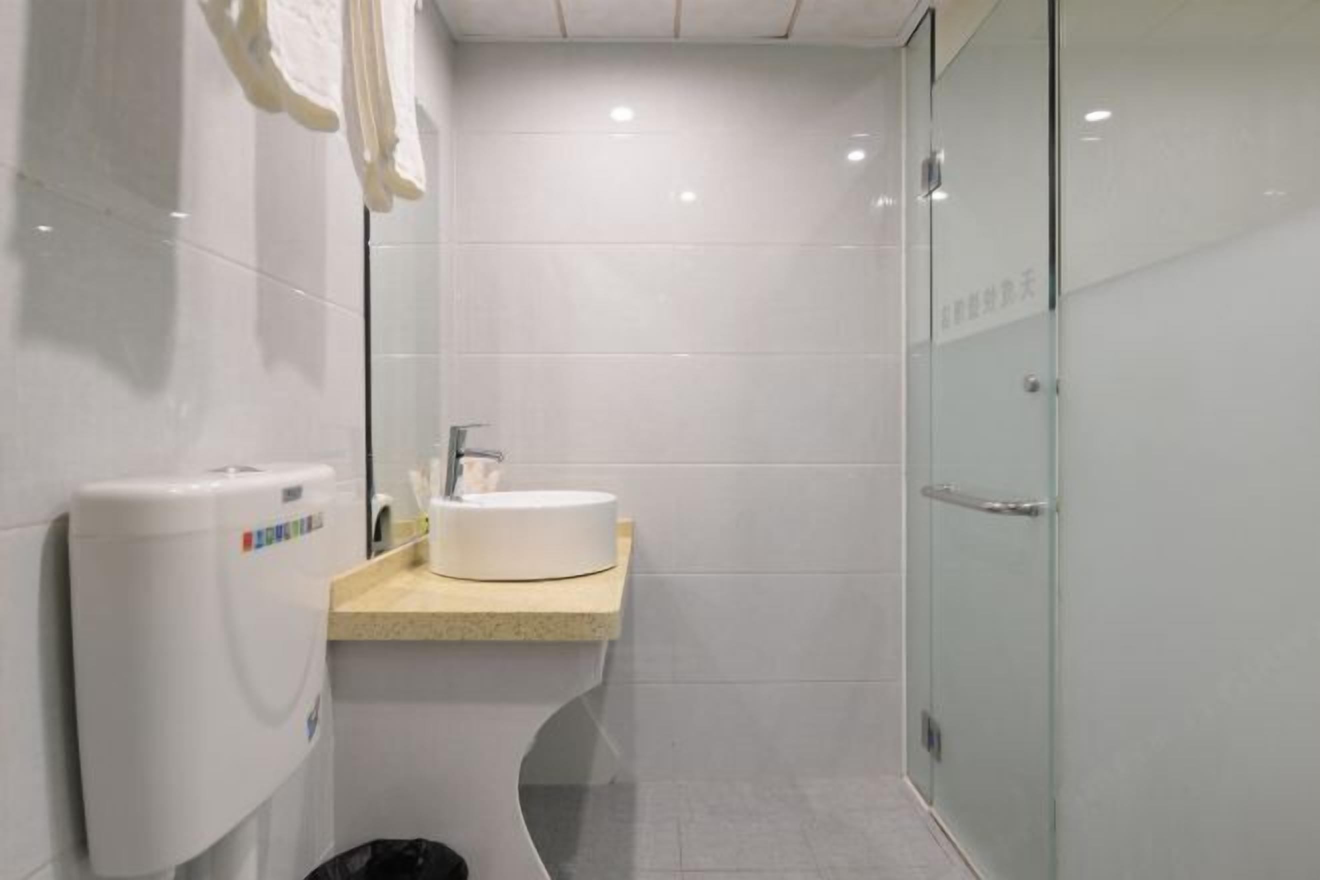 Casa de banho moderna com lavatório branco, secador de mãos e cabine de duche em vidro.