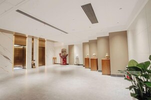Um hall amplo com piso de mármore, uma escultura vermelha no centro e uma planta à direita.
