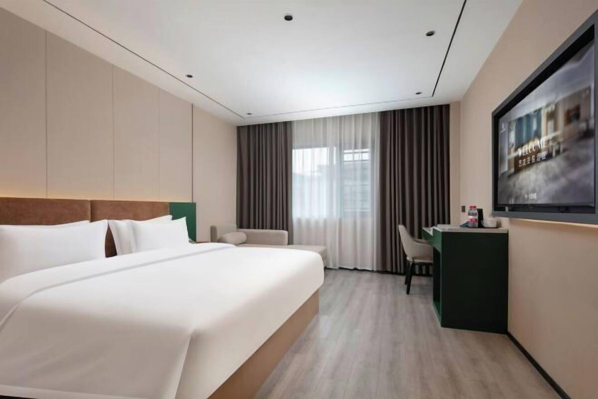 Quarto de hotel moderno com uma cama grande, uma escrivaninha, uma cadeira e uma TV fixada na parede.