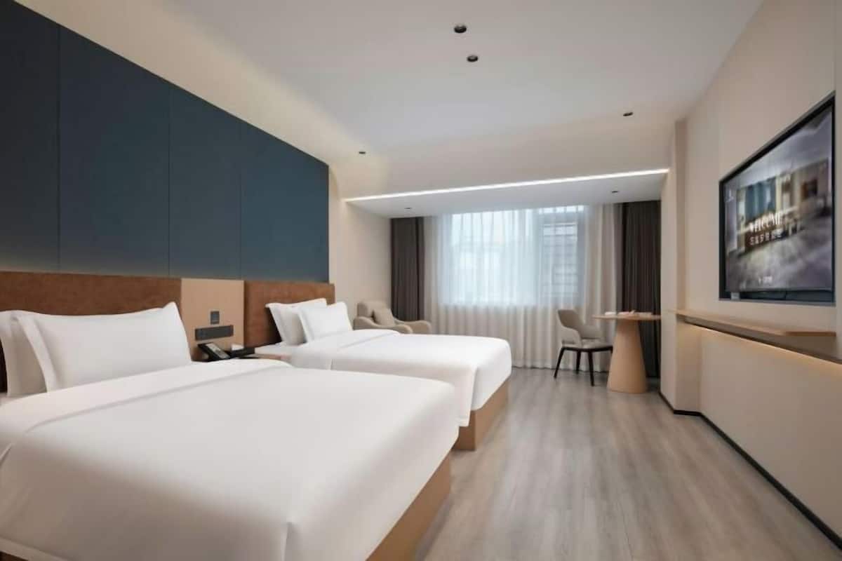 Quarto de hotel com duas camas, uma mesa e uma janela grande.
