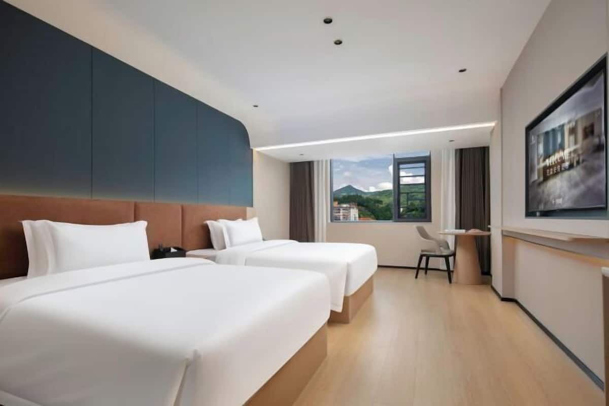 Quarto de hotel com duas camas, uma escrivaninha e uma janela com vista para as montanhas.