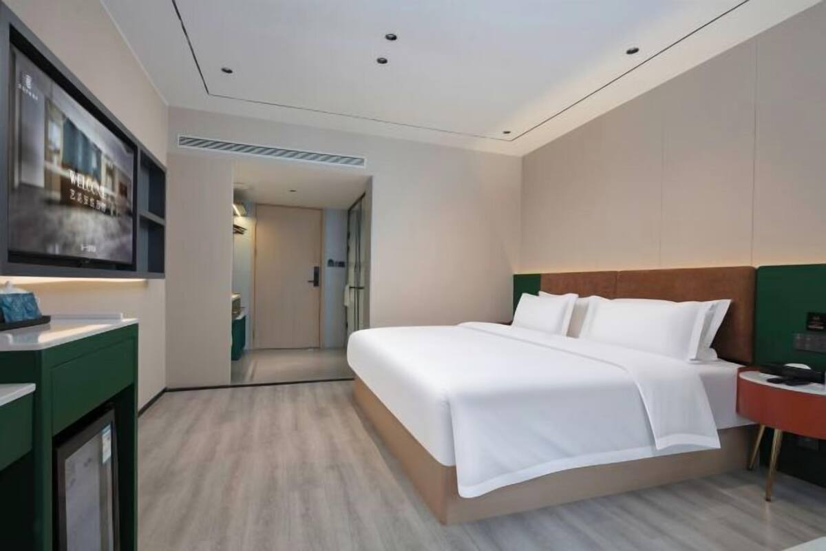 Quarto de hotel moderno com uma cama grande, uma escrivaninha com computador e televisão na parede.