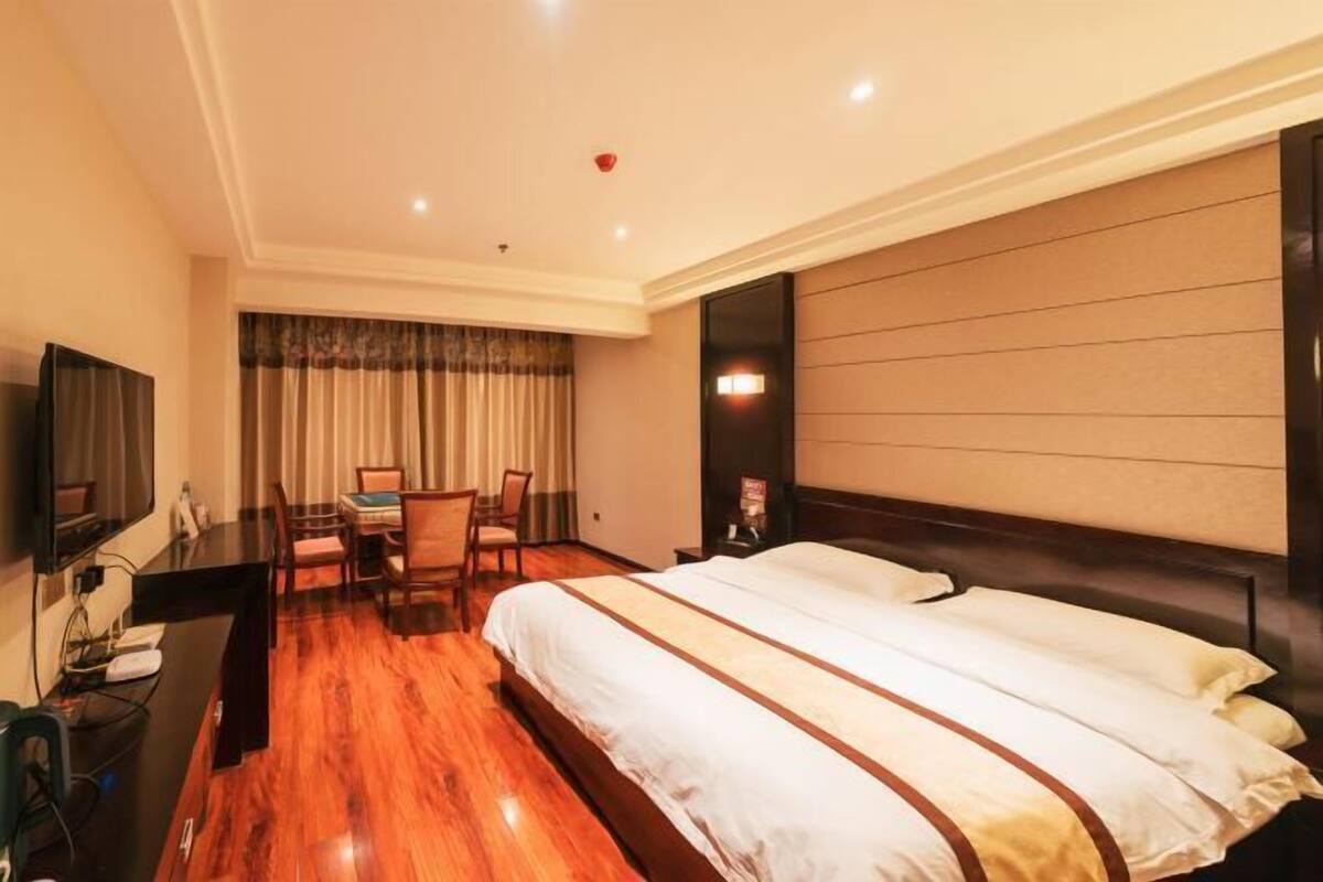 Quarto de hotel com cama grande, escrivaninha com cadeira, televisão e janela com cortinas.