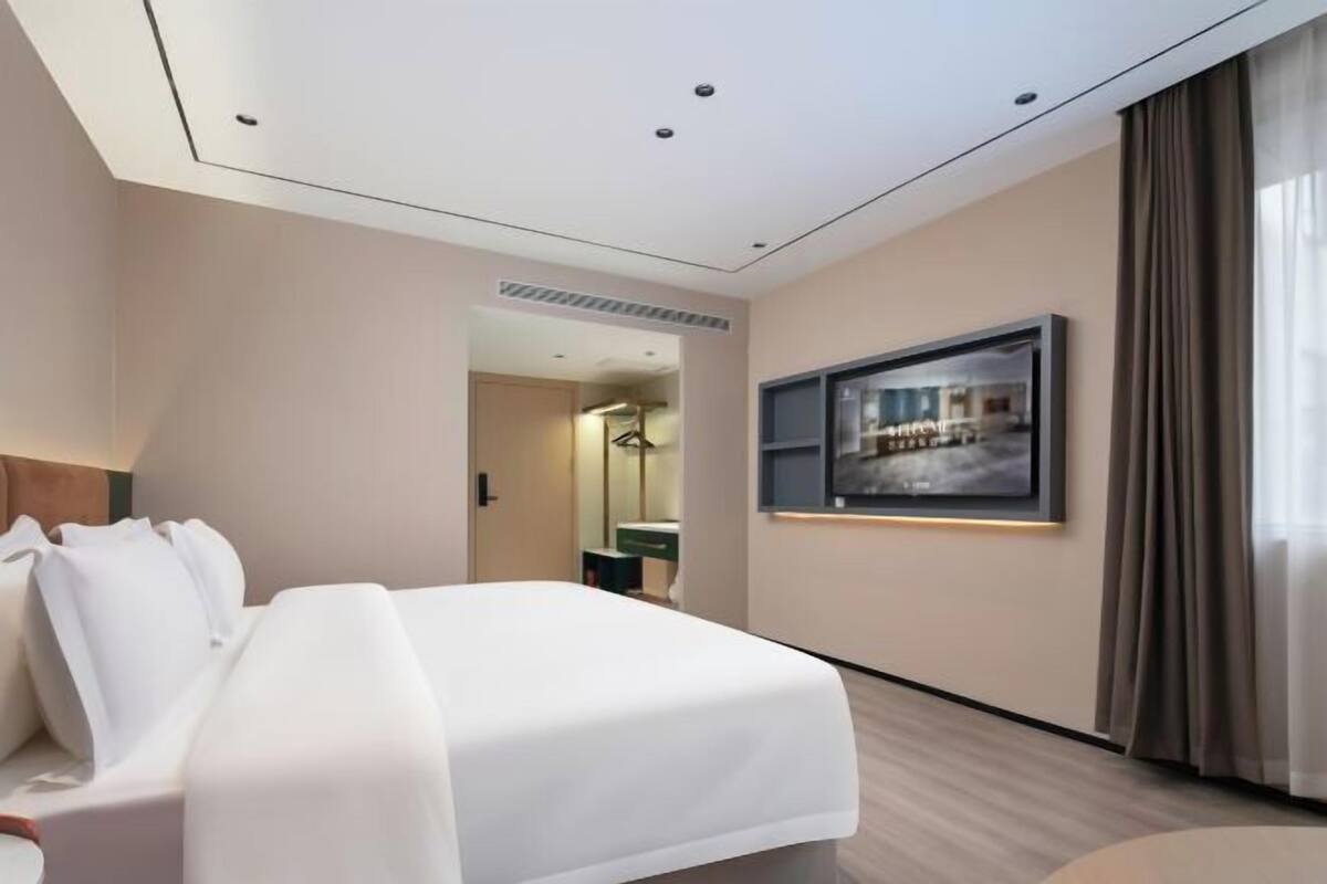 Quarto de hotel com uma cama, televisão na parede e uma janela com cortinas.