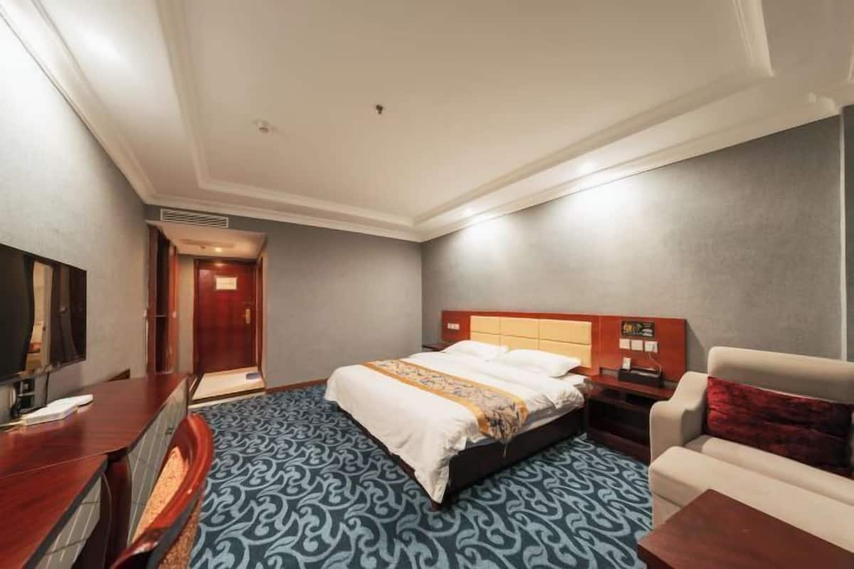 Quarto de hotel com uma cama grande, escrivaninha, cadeira e televisão.