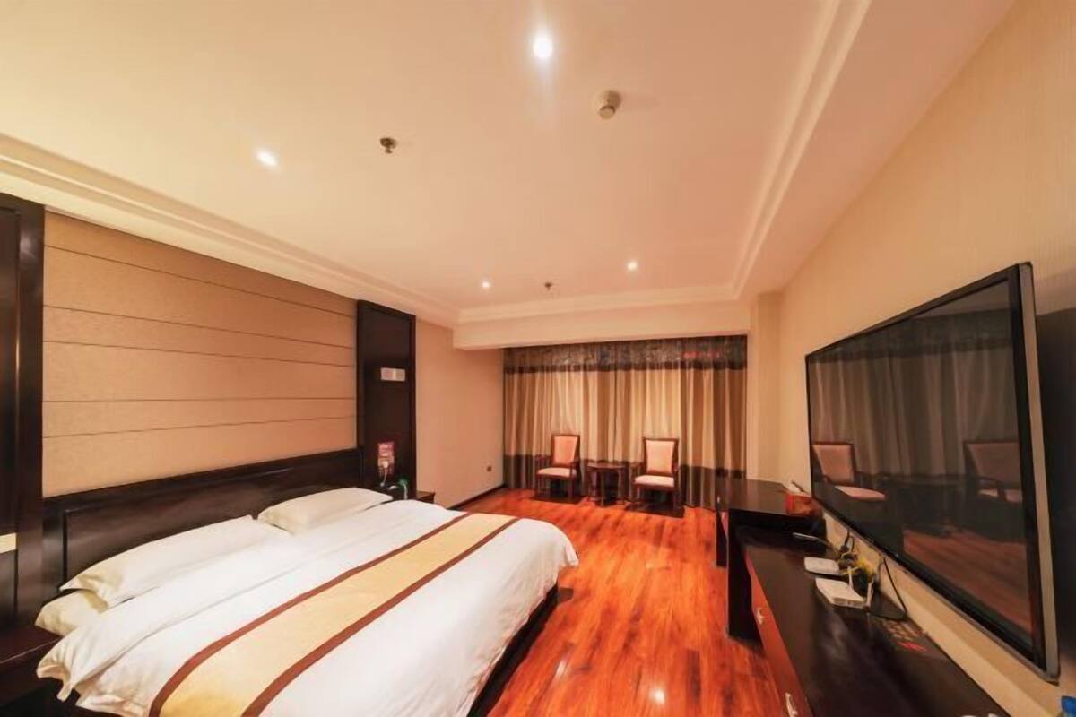 Quarto de hotel com uma cama grande, televisão de tela plana, escrivaninha com cadeira e janela com cortinas.