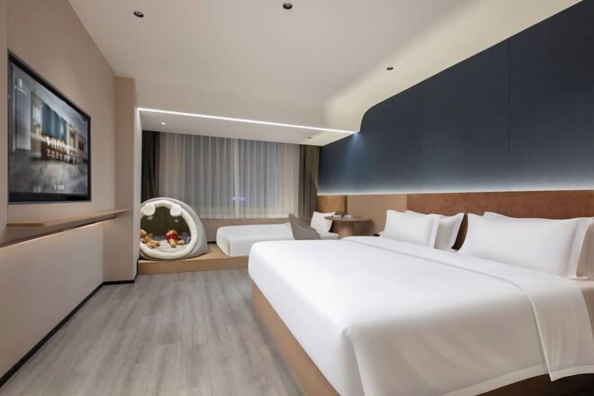 Quarto de hotel moderno com uma cama grande, área de estar com mesa redonda e televisão na parede.