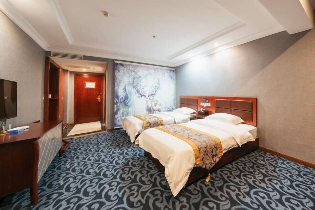 Quarto de hotel com duas camas, uma escrivaninha e uma janela grande.