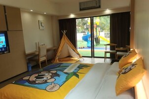 Quarto de hotel com cama, televisão, escrivaninha, cadeira, uma tenda e vista para um parquinho.
