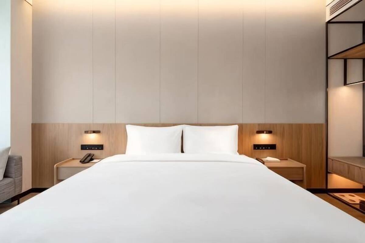 Quarto de hotel com uma cama grande, duas mesas de cabeceira com luminárias, cabeceira de madeira e um banco embutido.