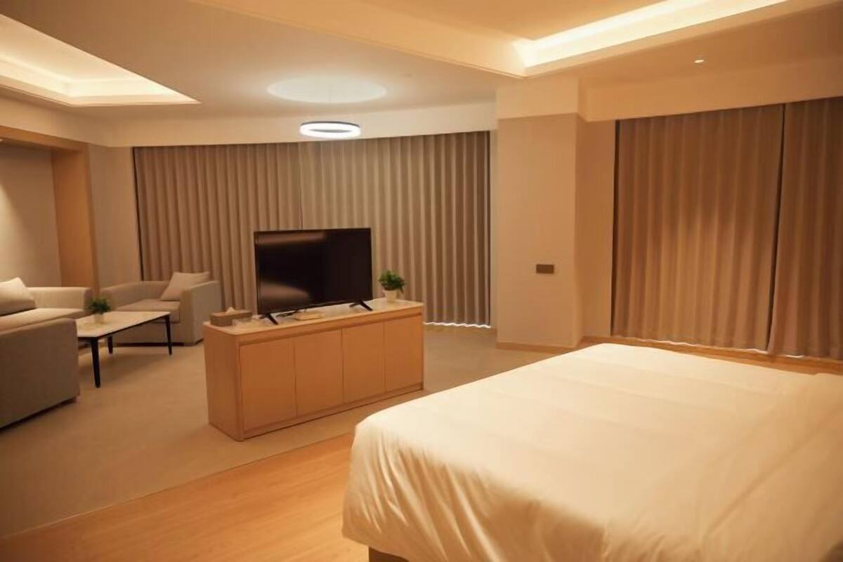 Quarto de hotel moderno com uma cama grande, televisão de tela plana, sofá, mesa de centro e aparador para TV.