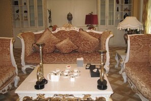 Um quarto com um sofá estampado, uma mesa com jogos de chá e um armário com portas de vidro.